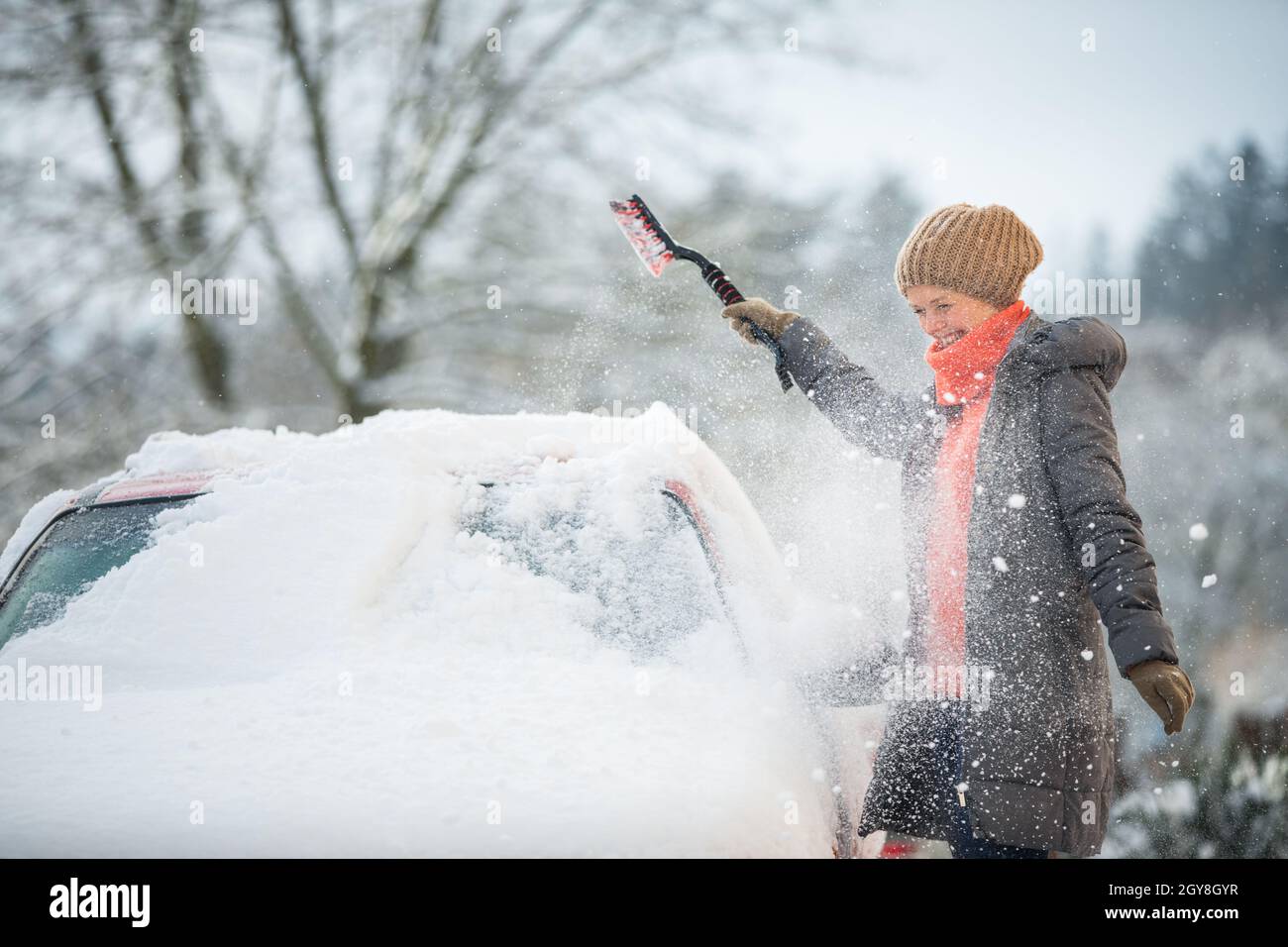 Pretty, young woman cleaning her car from snow after heavy snowstorm ...