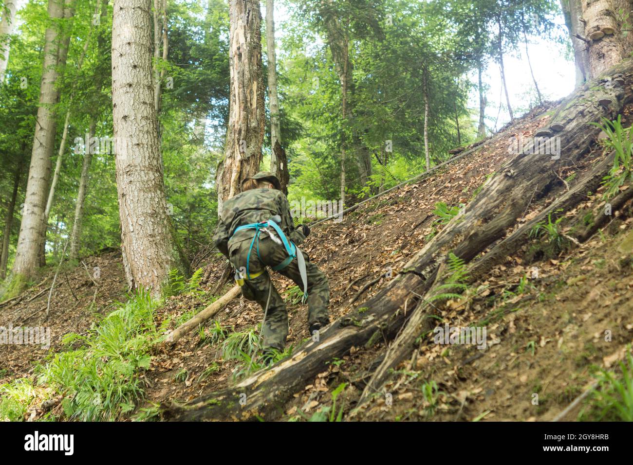 A young soldier in military outfit climbing on a steep slope in ...