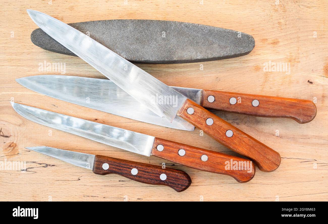 top view of used kitchen knives and sharpening stone on wooden board ...