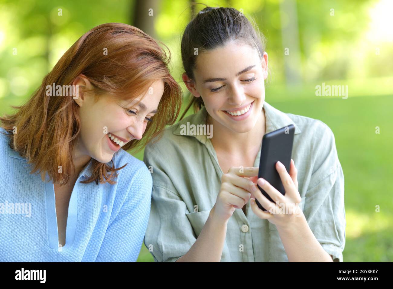 Two happy friends laughing loud checking smart phone in a park Stock ...