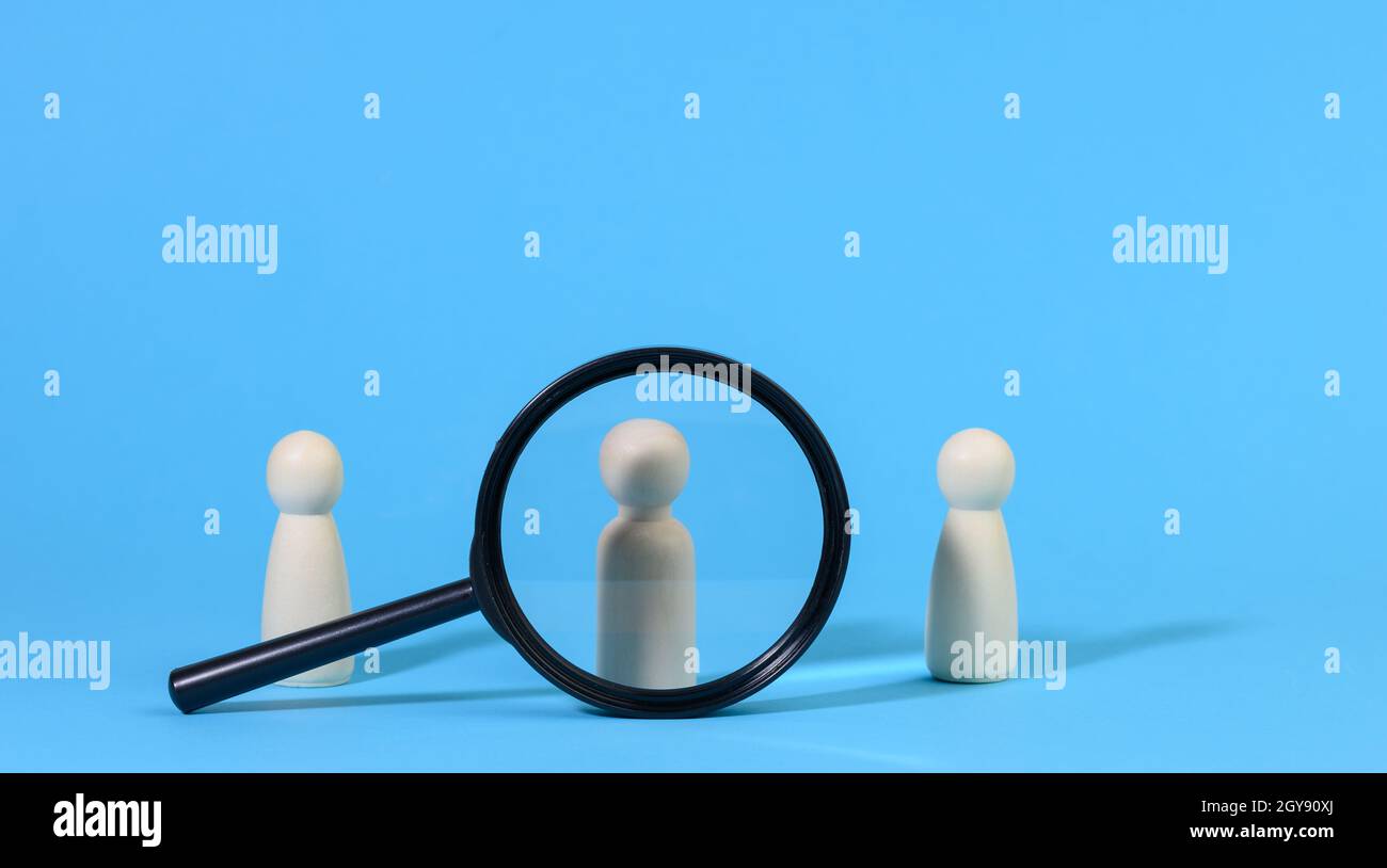 wooden figures of men stand on a blue background and a black magnifying ...