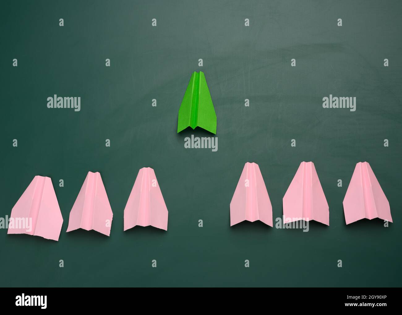 group of pink paper planes follow the first green airplane against a ...