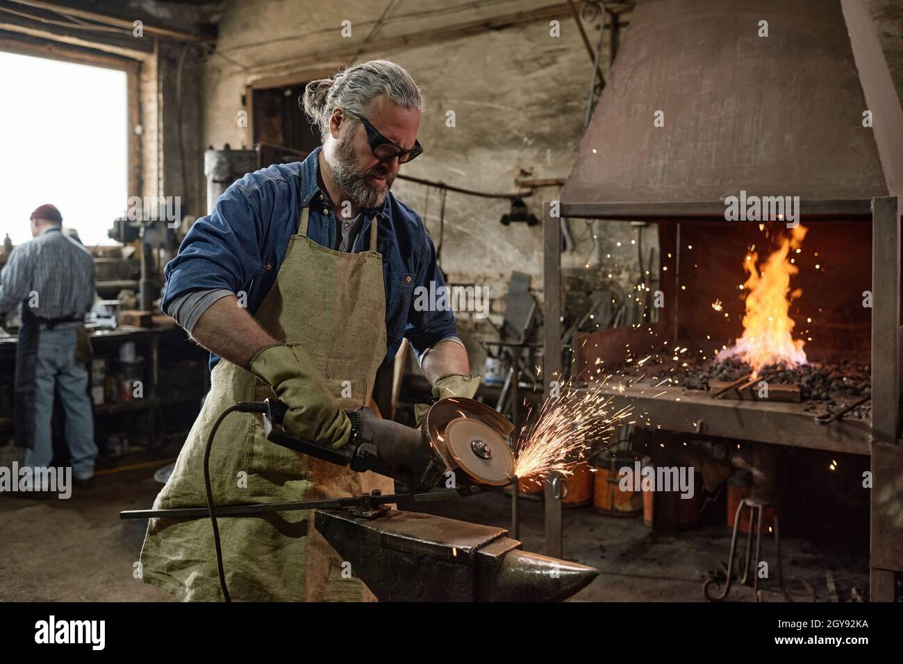 Mature carpenter in apron using grinder to make detail from metal ...