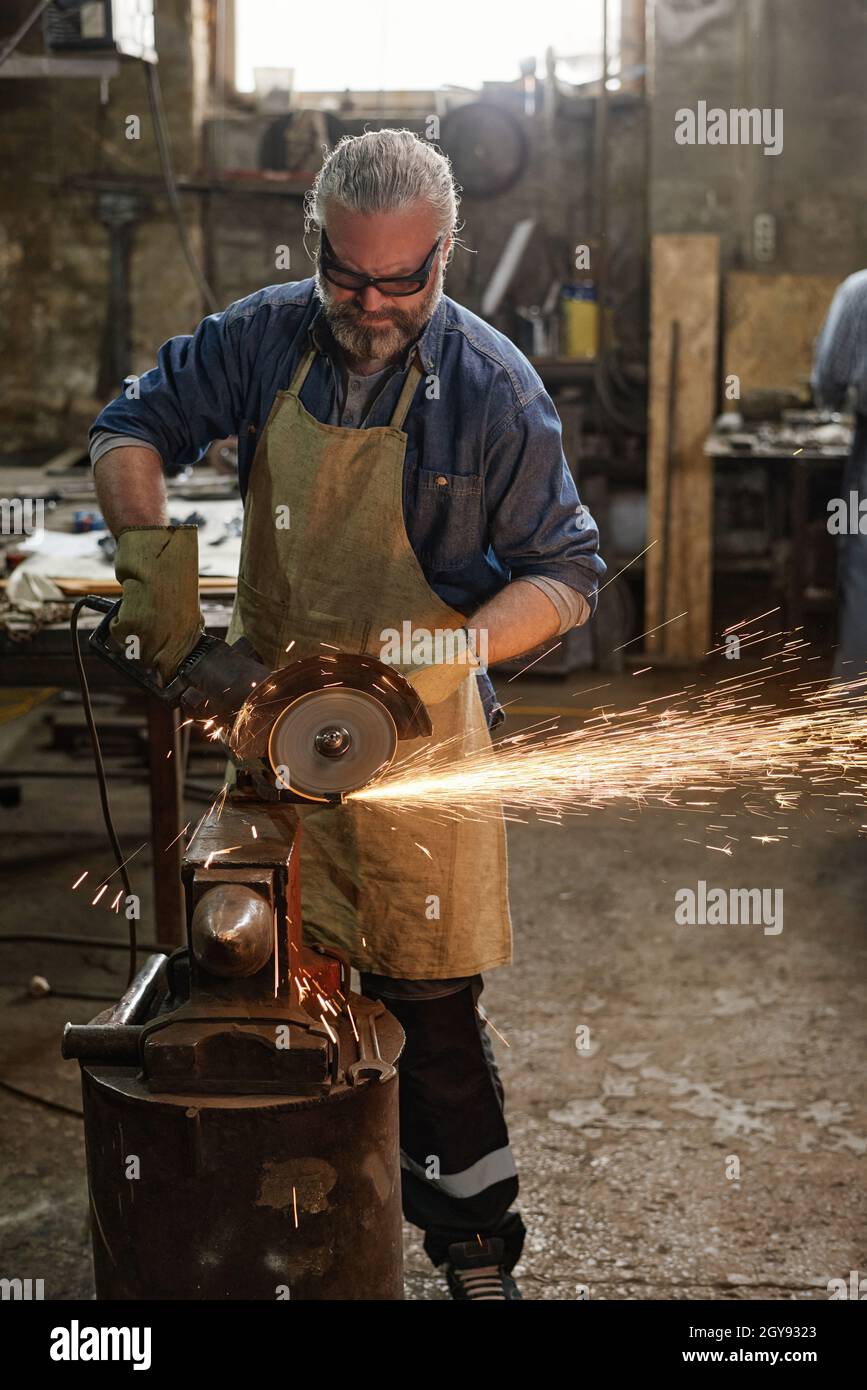 Mature worker using hand saw to polish metallic detail during his work ...