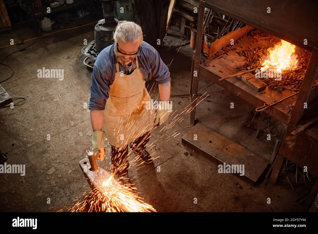 High angle view of mature man in apron forging the metal in the ...