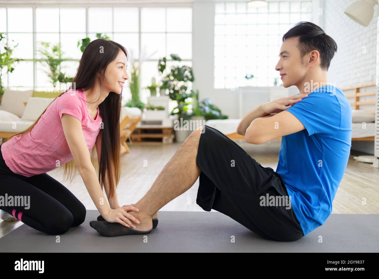 Young woman helping young man to do crunches at home Stock Photo - Alamy