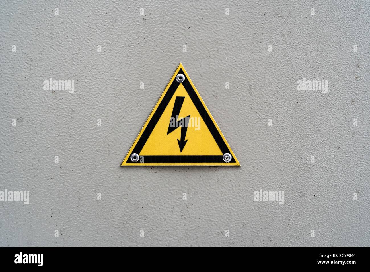 High voltage yellow triangle warning sign on gray metal wall. Danger ...