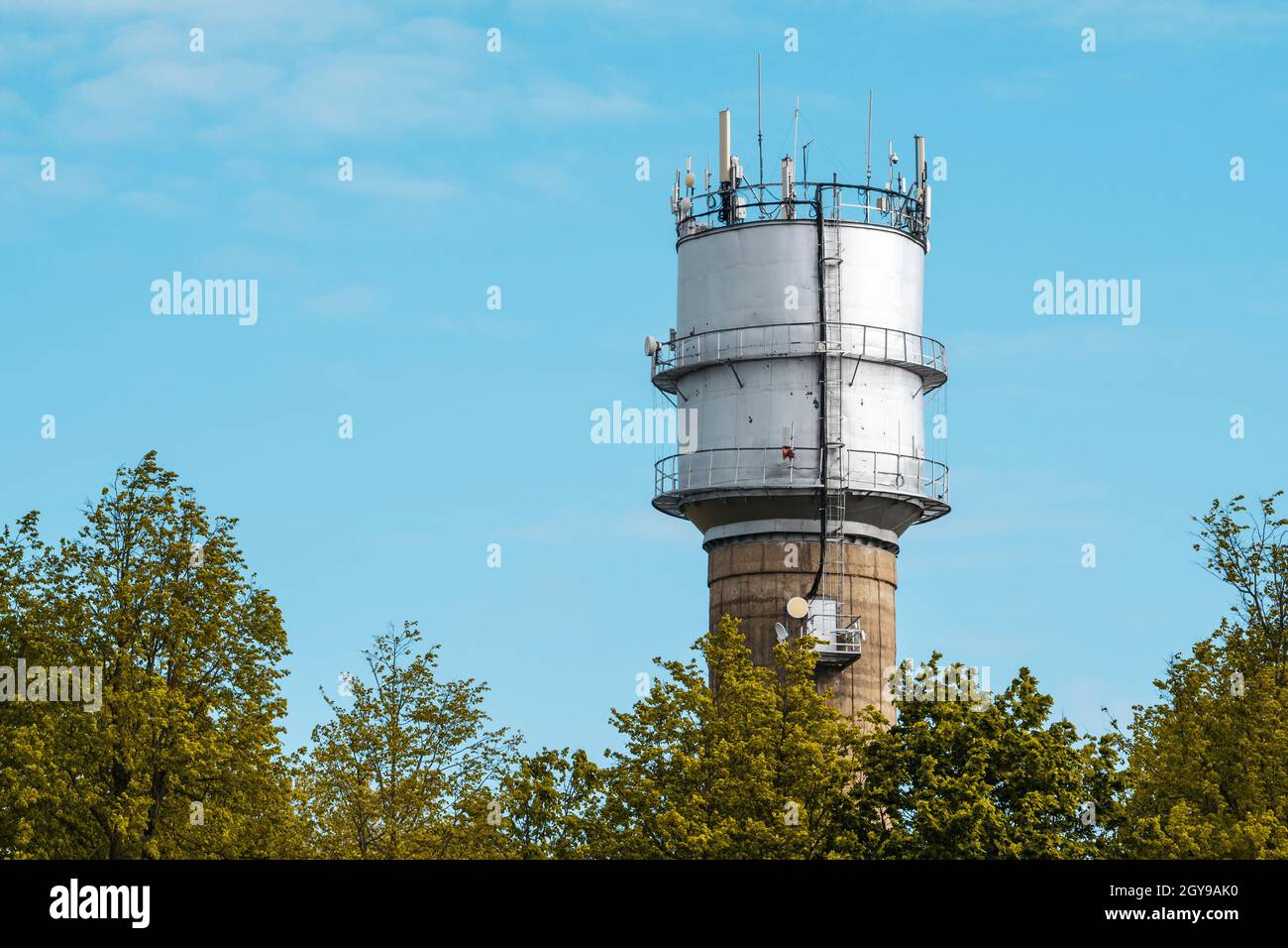 Tall water tower with communication antennas over a green tree tops ...