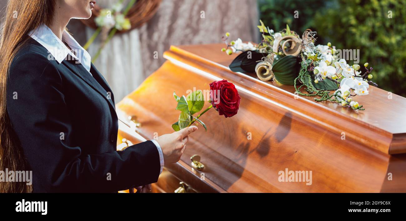 Mourning woman on funeral with red rose standing at casket or coffin ...