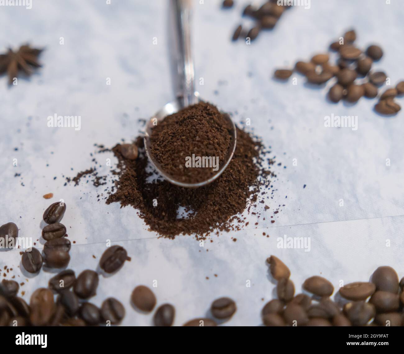 Spoonful of coffee surrounded by piles of coffee beans on white surface ...
