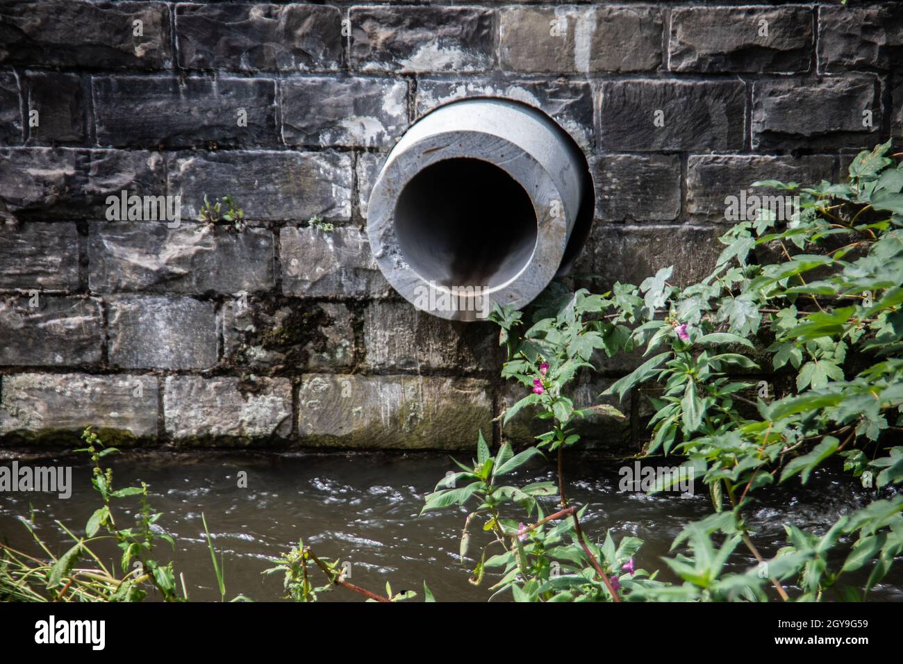 Sewer pipe in natural stone wall flows into the river Stock Photo - Alamy