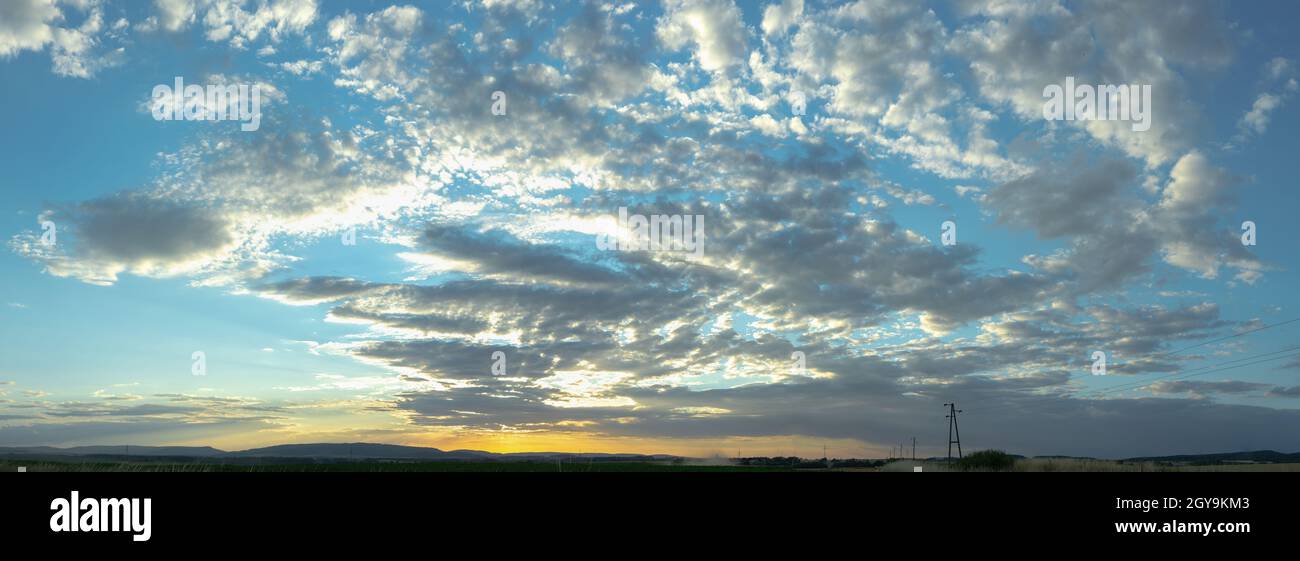 Panorama view on a moody yellow sunset between the clouds sky Stock Photo - Alamy