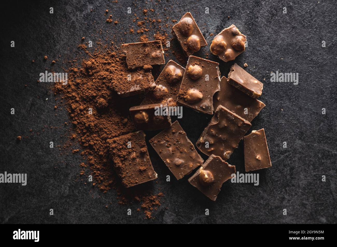 Nutty chocolate with hazelnuts and cocoa powder on black table. Top ...