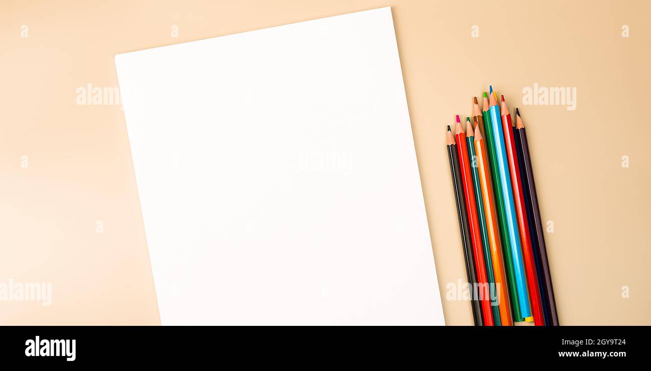 A blank white sheet and colored pencils for drawing on a plain textured ...