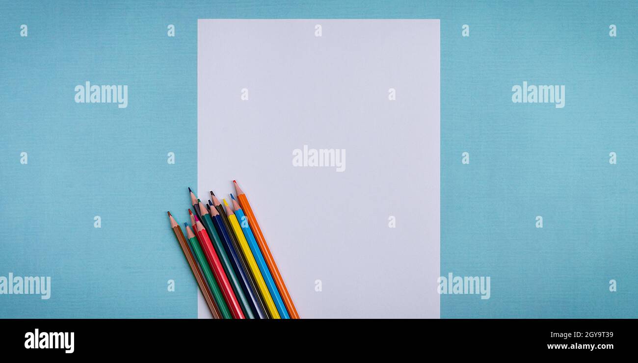 A blank white sheet and colored pencils for drawing on a plain textured ...