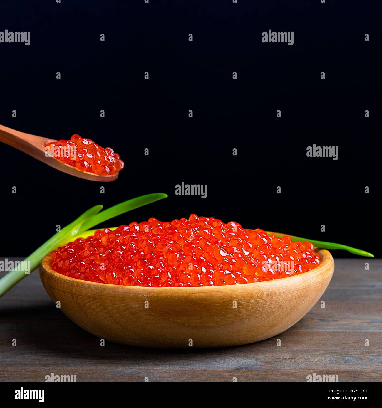 Red caviar in a wooden cup on a black background with a spoon and green ...