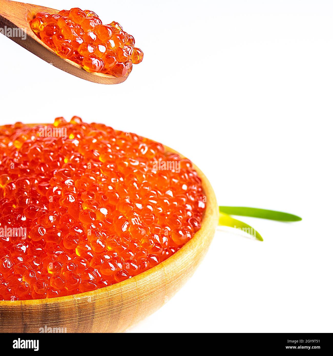 Red caviar in a wooden cup on a white background with a spoon and green ...