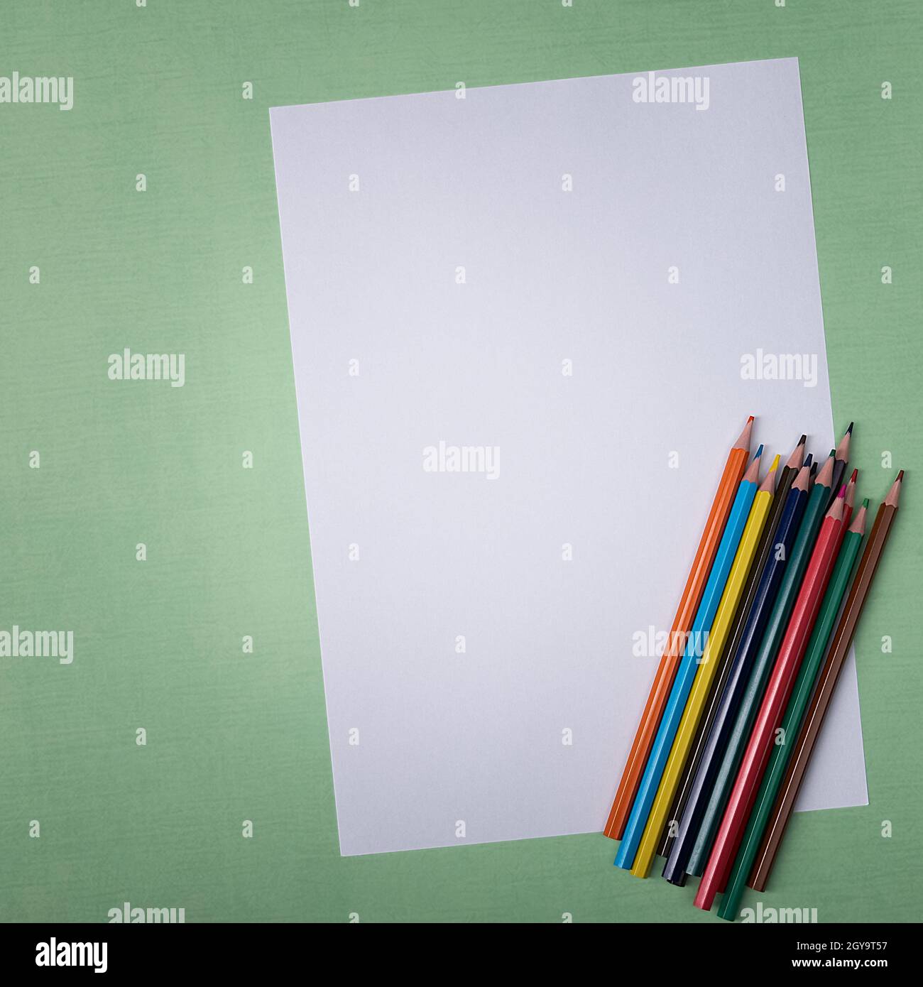 A blank white sheet and colored pencils for drawing on a plain textured ...