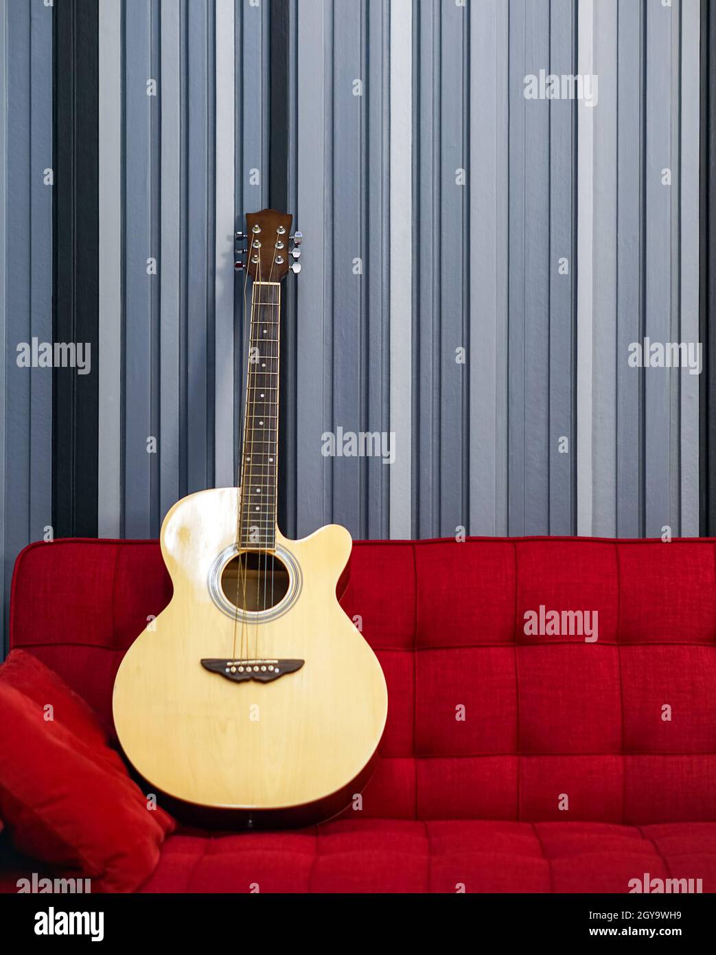 Acoustic guitar on red couch in front of modern gray galvanized steel ...
