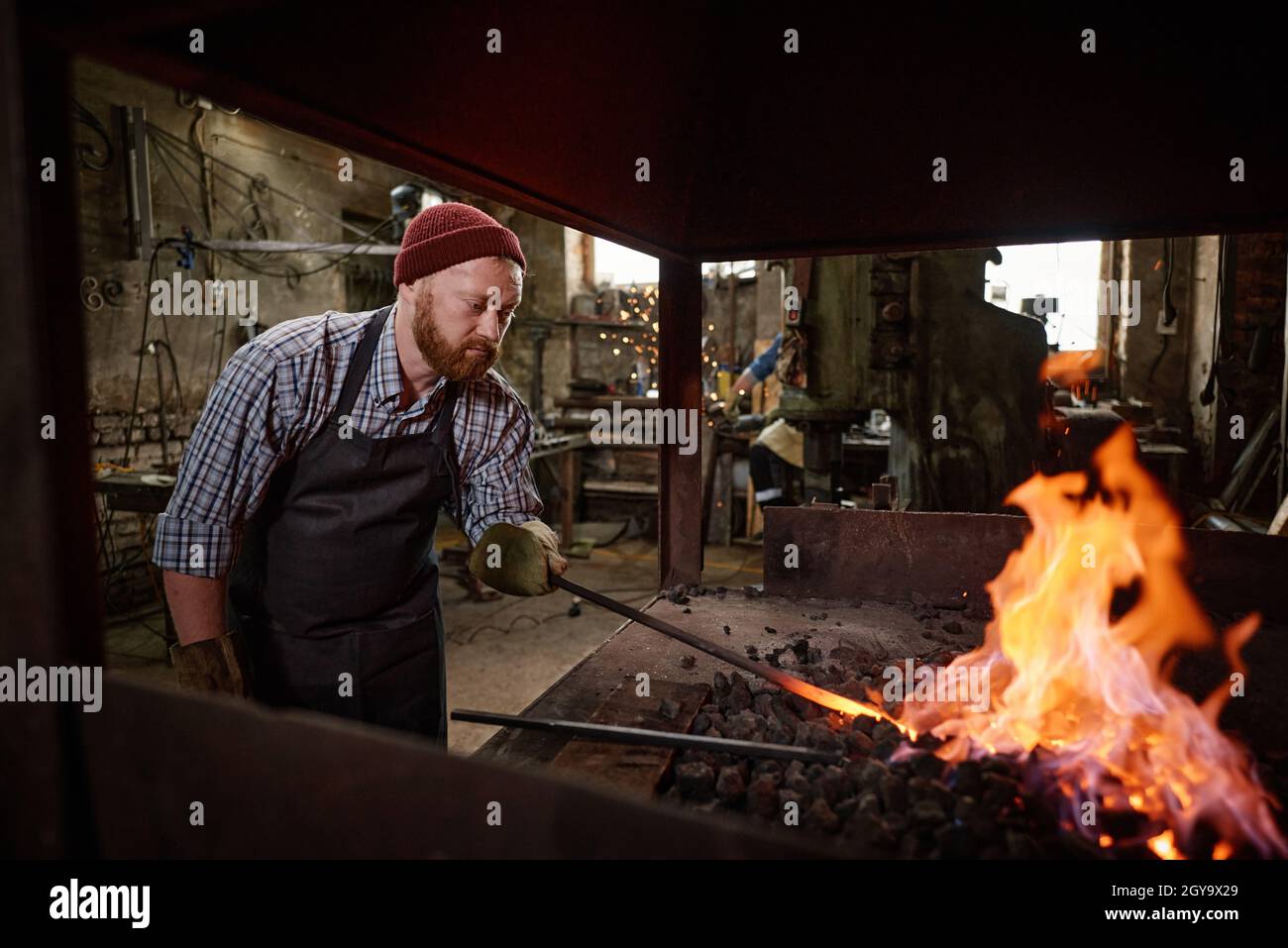 Worker in the apron burning the flame with coals in the furnace while ...