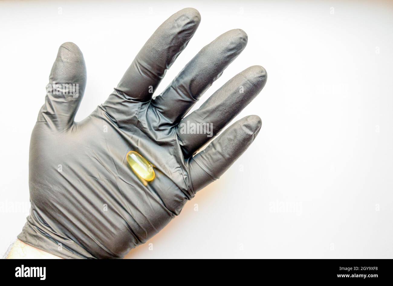 one yellow capsule of fish oil in hand in a black medical glove on a ...