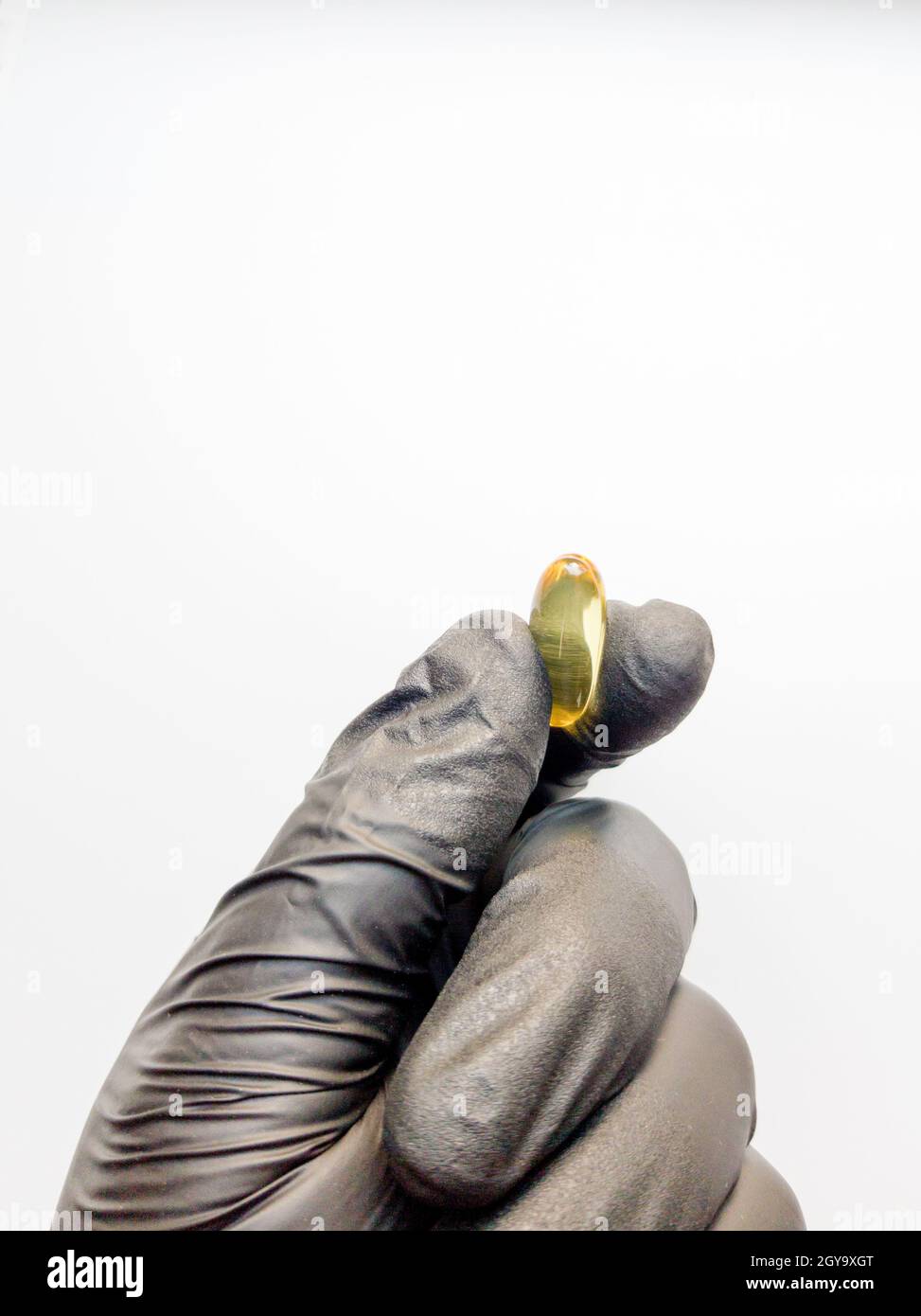 one yellow capsule of fish oil in hand in a black medical glove on a ...