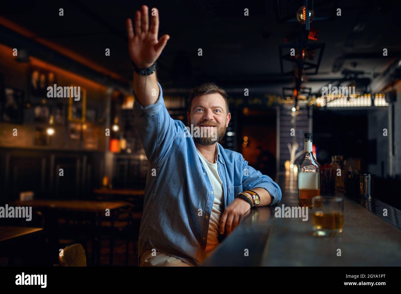 Bearded man with raised hand sitting at the counter in bar. One male ...