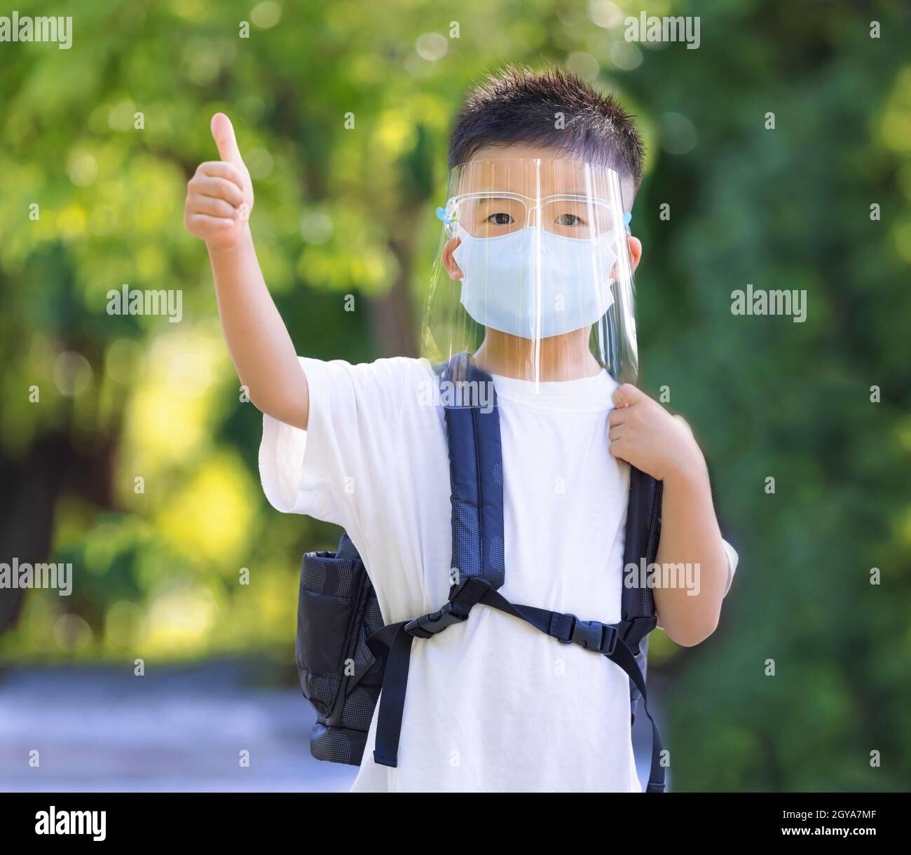 Happy little boy student wearing mask and face shield . showing thumbs ...