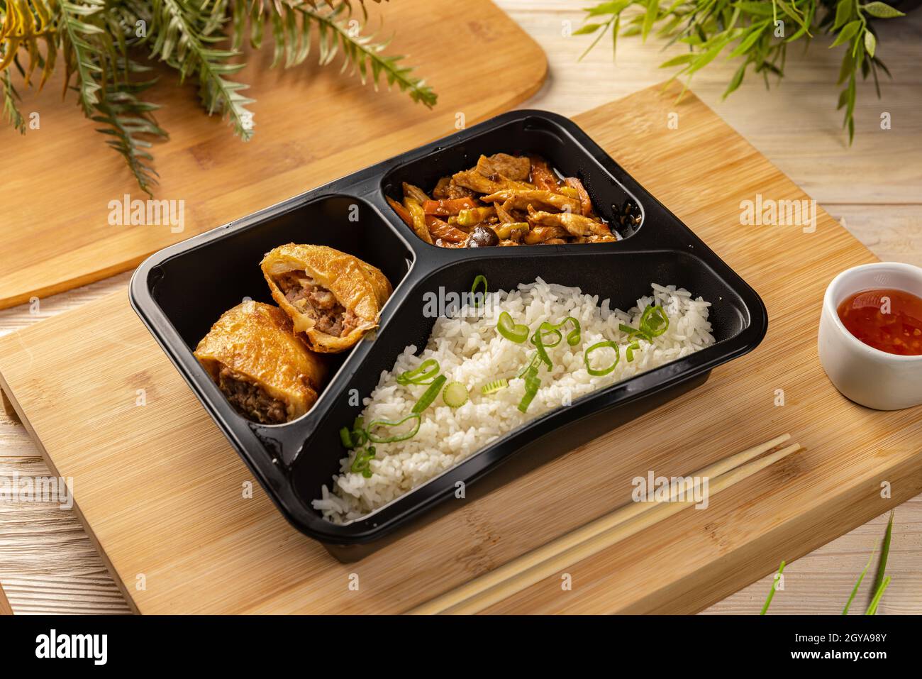 Rice with pork roll and chicken stew in take-out box on bamboo chopping ...