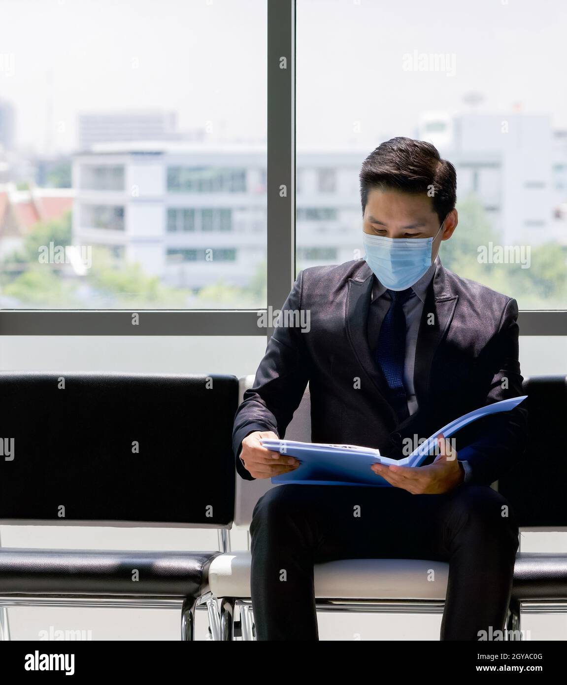 Asian business man in black suit and face mask sit on a bench near the ...
