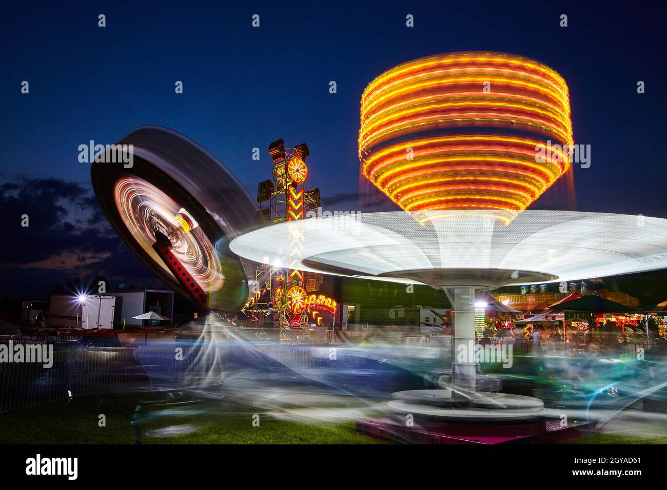Spinning rides and brilliant lights at a carnival or fair at dusk Stock ...
