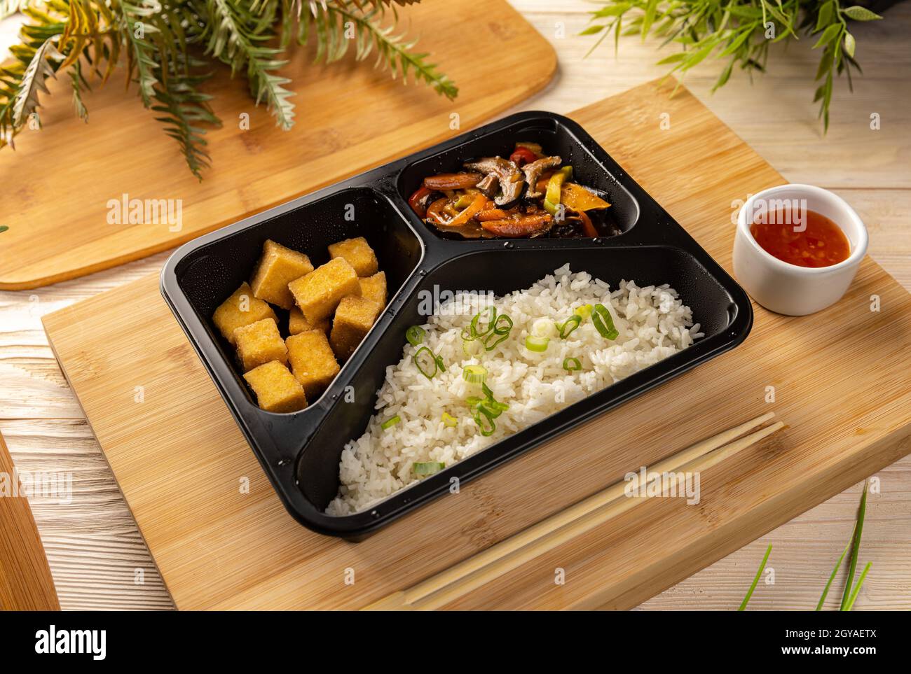 Rice with tofu and vegetable stew in take-out box on bamboo chopping ...