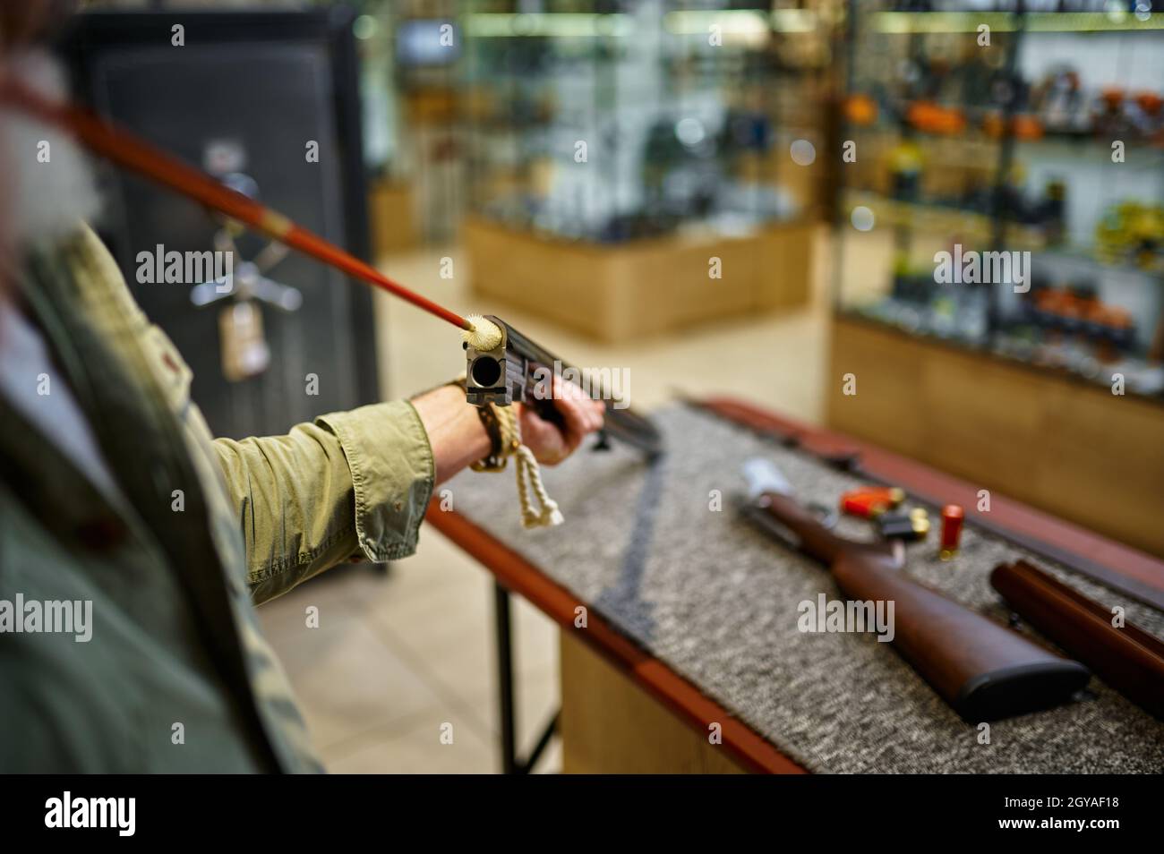 Male hunter with ramrod cleans rifle in gun store. Weapon shop interior ...