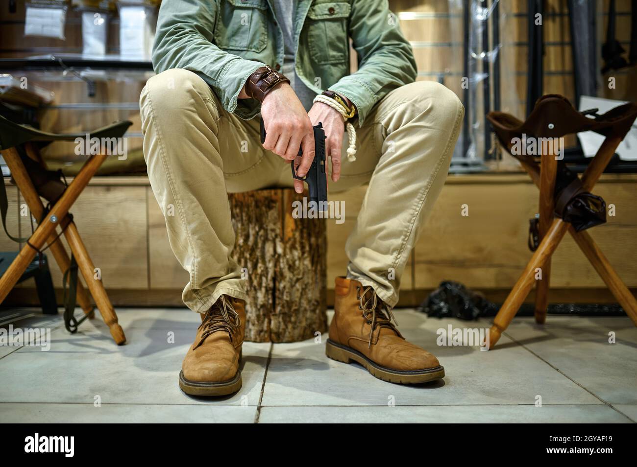 Man with pistol sitting on stump in gun store. Weapon shop interior ...