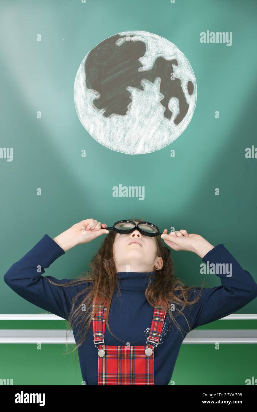 Pre-adolescent girl looks at the drawn moon through a magnifying glass ...