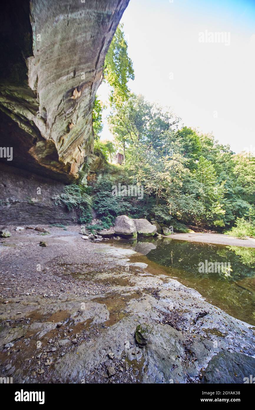 Shallow waterfall basin with overhanging cliff edge in a green forest ...
