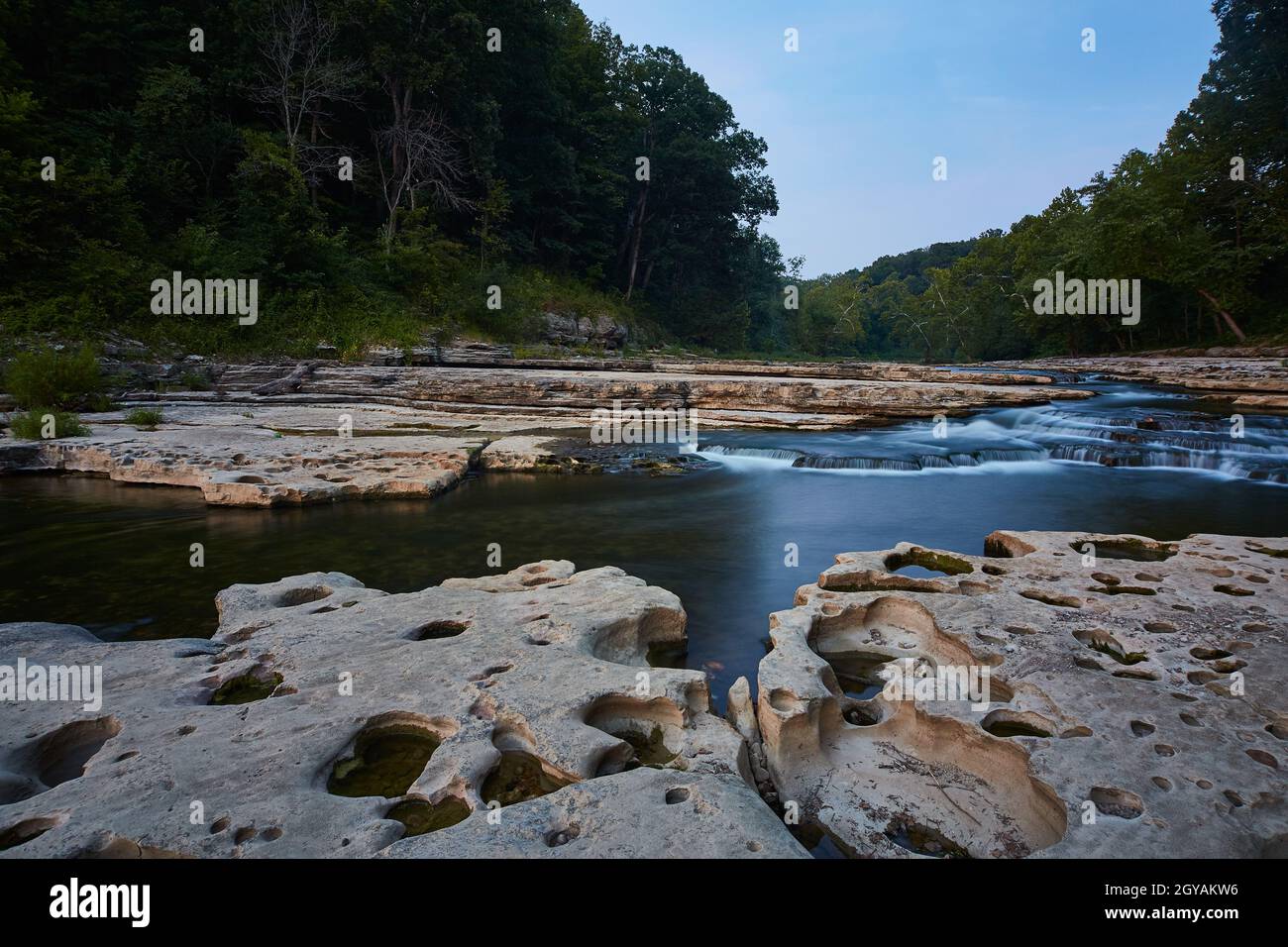 River with giant flat rocks and small waterfalls with a green forest at ...