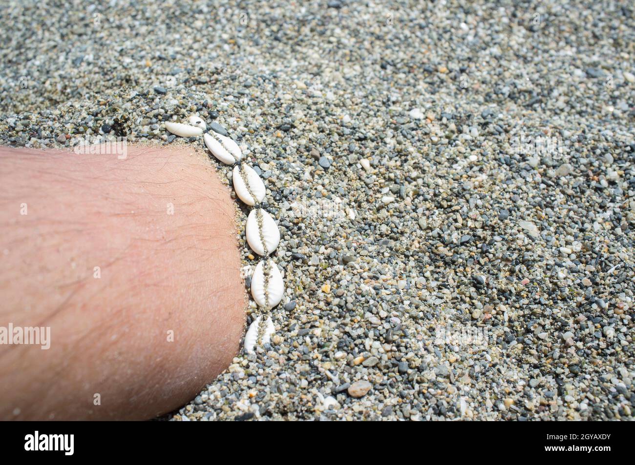 Shell ankle bracelet on half buried male leg. Symbol of summertime ...