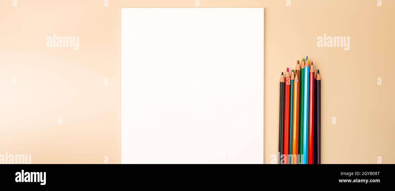 A blank white sheet and colored pencils for drawing on a plain textured ...