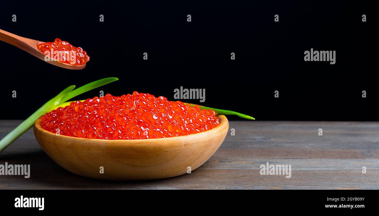 Red caviar in a wooden cup on a black background with a spoon and green ...