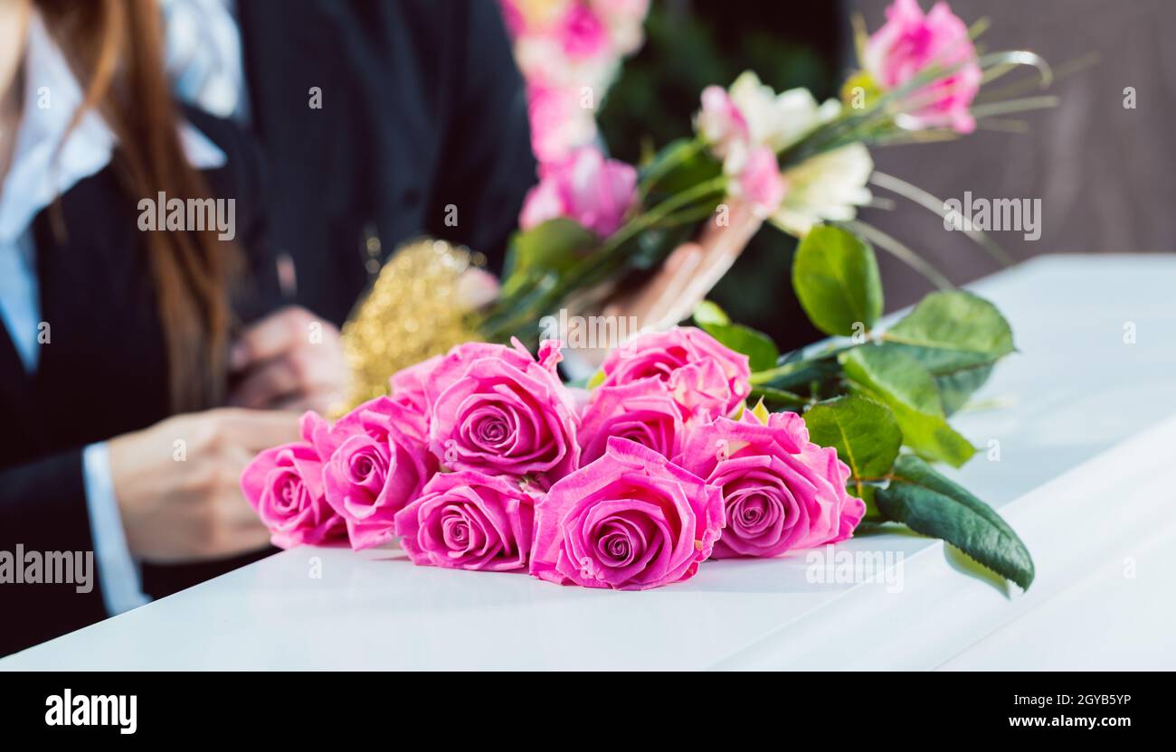 Mourning man and woman on funeral with pink rose standing at casket or ...