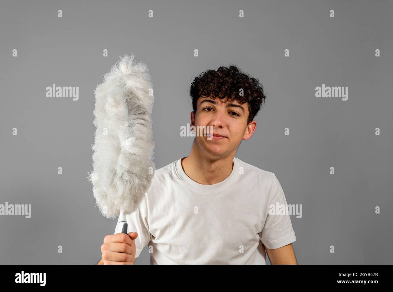 Caucasian young man posing funny with a cleaning duster on blue studio ...