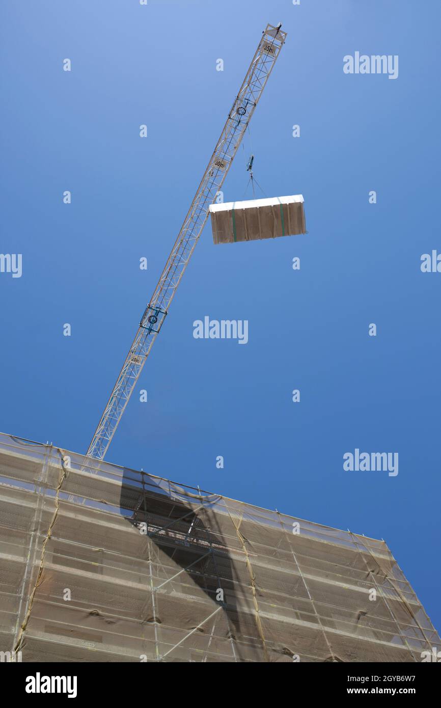Crane with load of drywall panels over construction site. Working Under ...