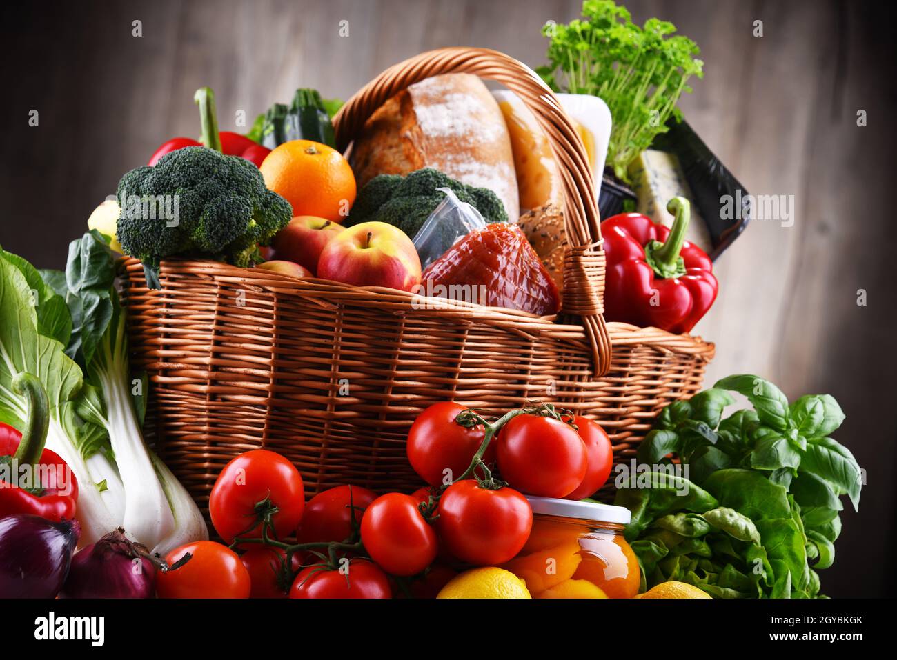 Wicker basket with assorted grocery products including fresh vegetables ...