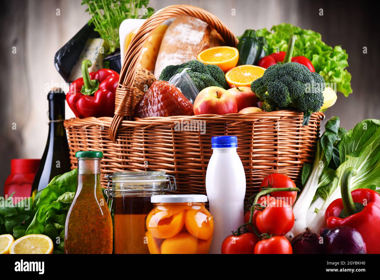 Wicker basket with assorted grocery products including fresh vegetables ...