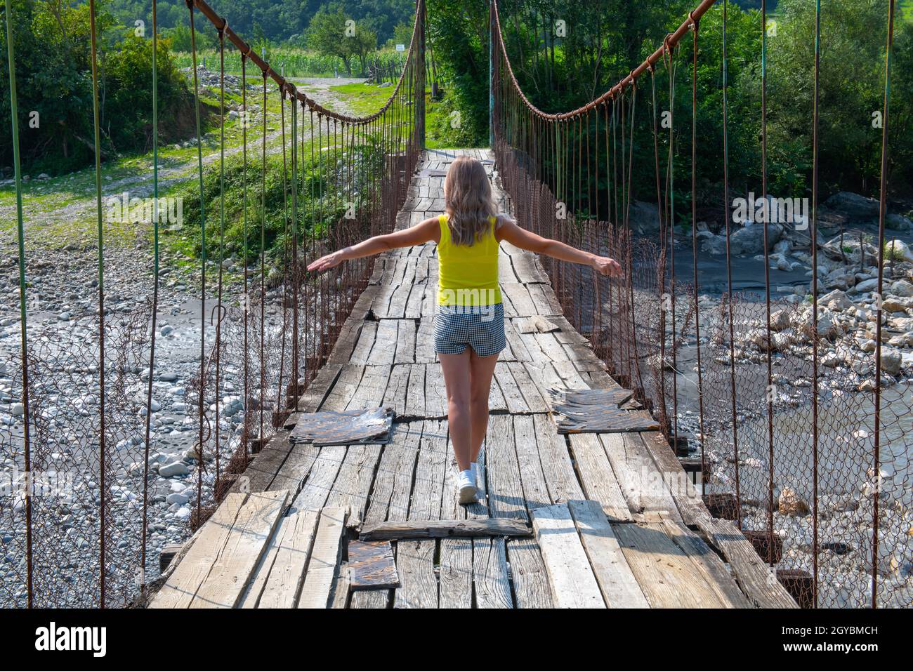 a girl in a yellow t-shirt is walking on a suspension bridge Stock ...