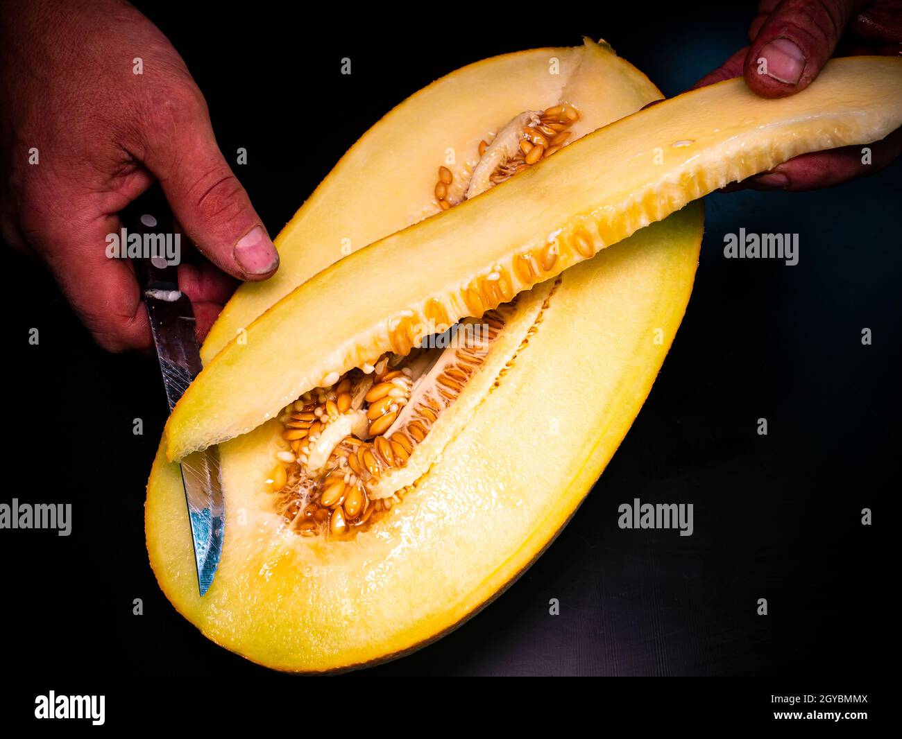A yellow melon cut with a knife in the hands of a man. Food photo ...