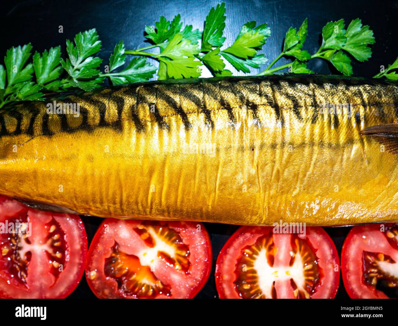 Smoked mackerel fish with tomatoes on a black background. Salted ...