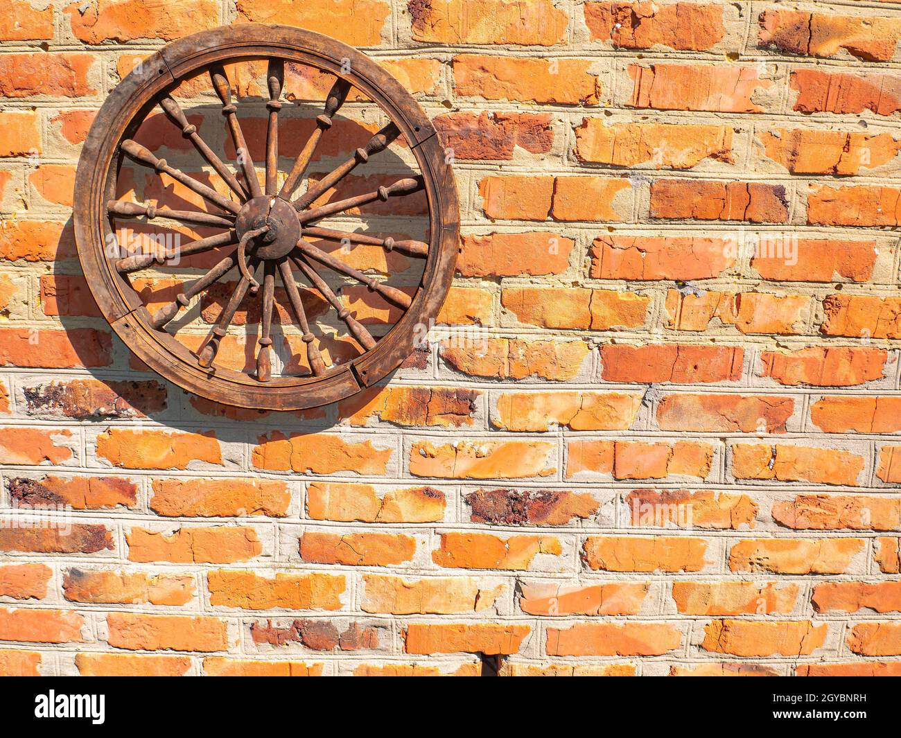 Old wooden wheel on a brick wall. Wooden wheel of a horse carriage. Red ...