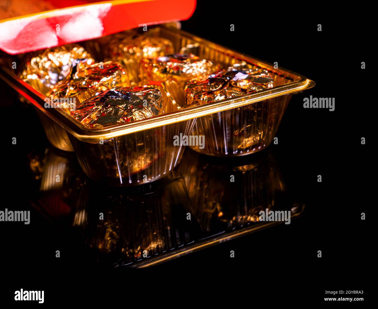 A box of round candies in golden foil on a black background. Wrapped ...